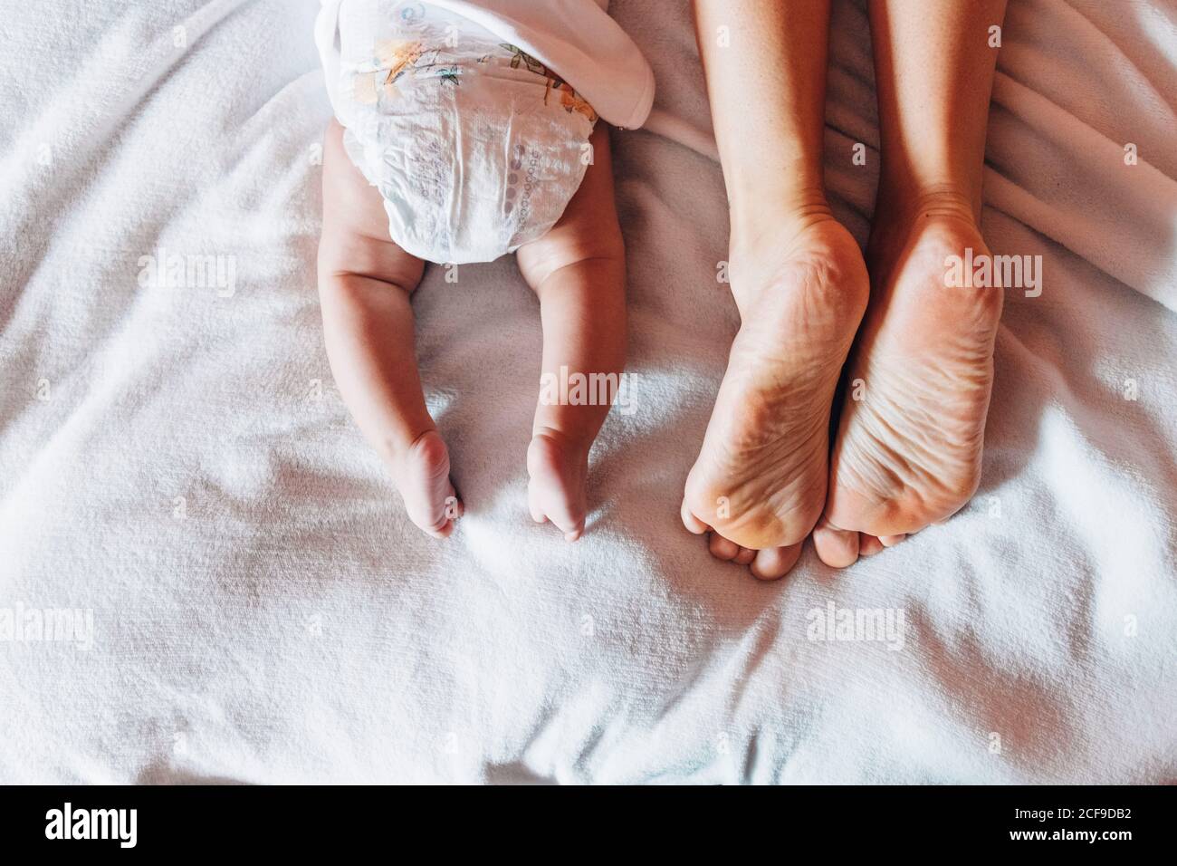Top view of crop newborn baby in diaper lying on bed with mother in ...