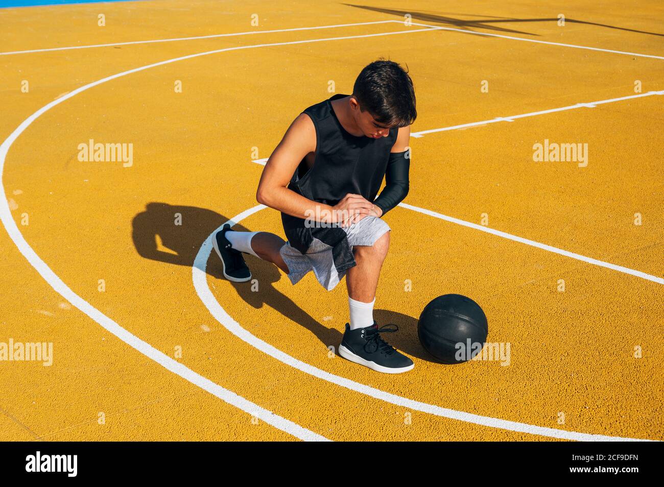 Young man and ball stretching on basketball court outdoor resting after ...