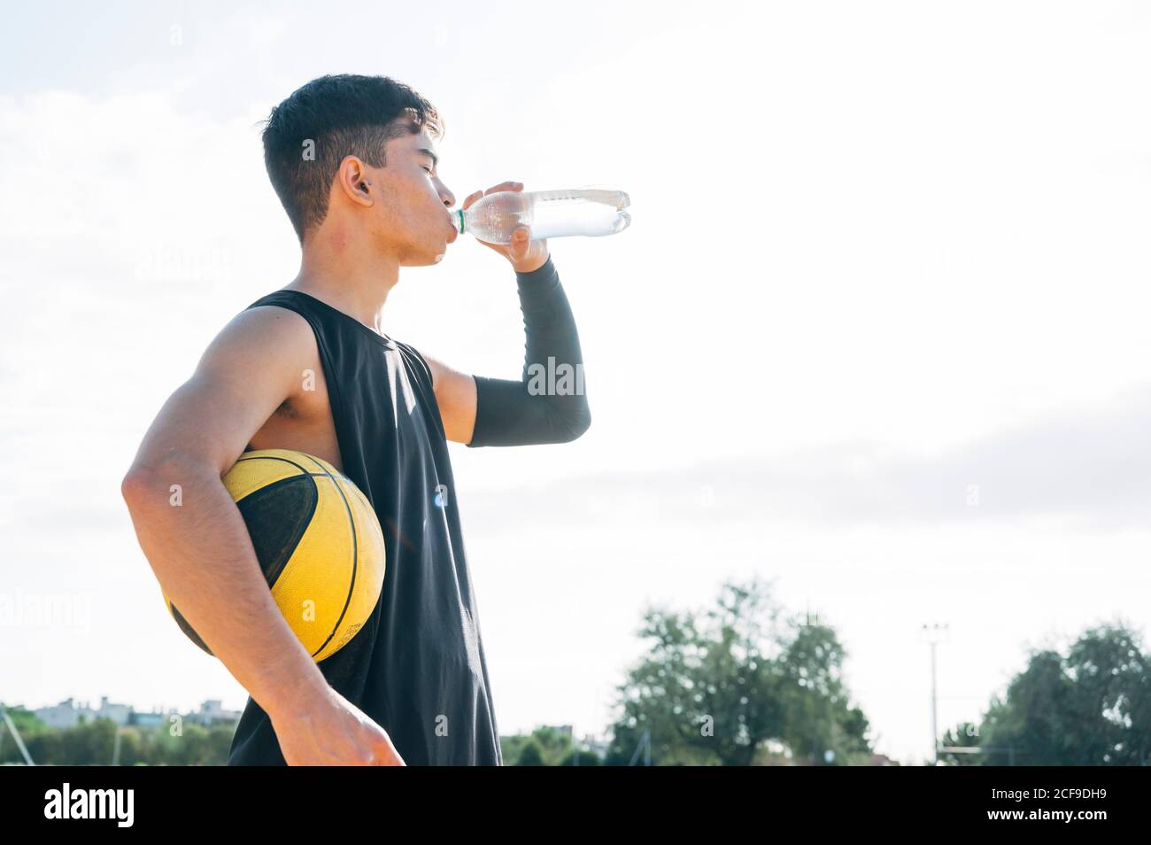 Young man playing on yellow basketball court outdoor drinking water ...