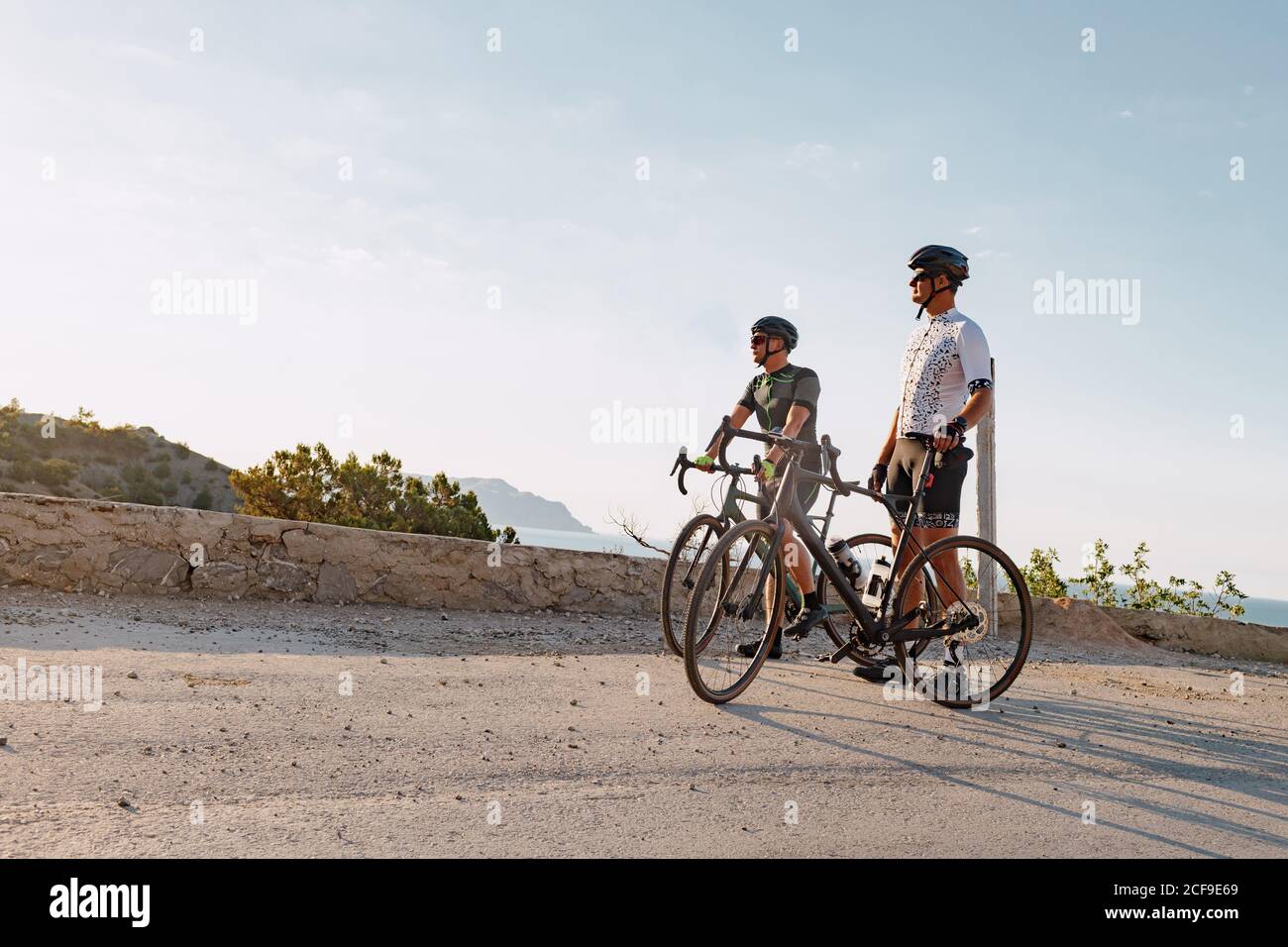 Two male cyclists stand on the road and have a rest Stock Photo - Alamy