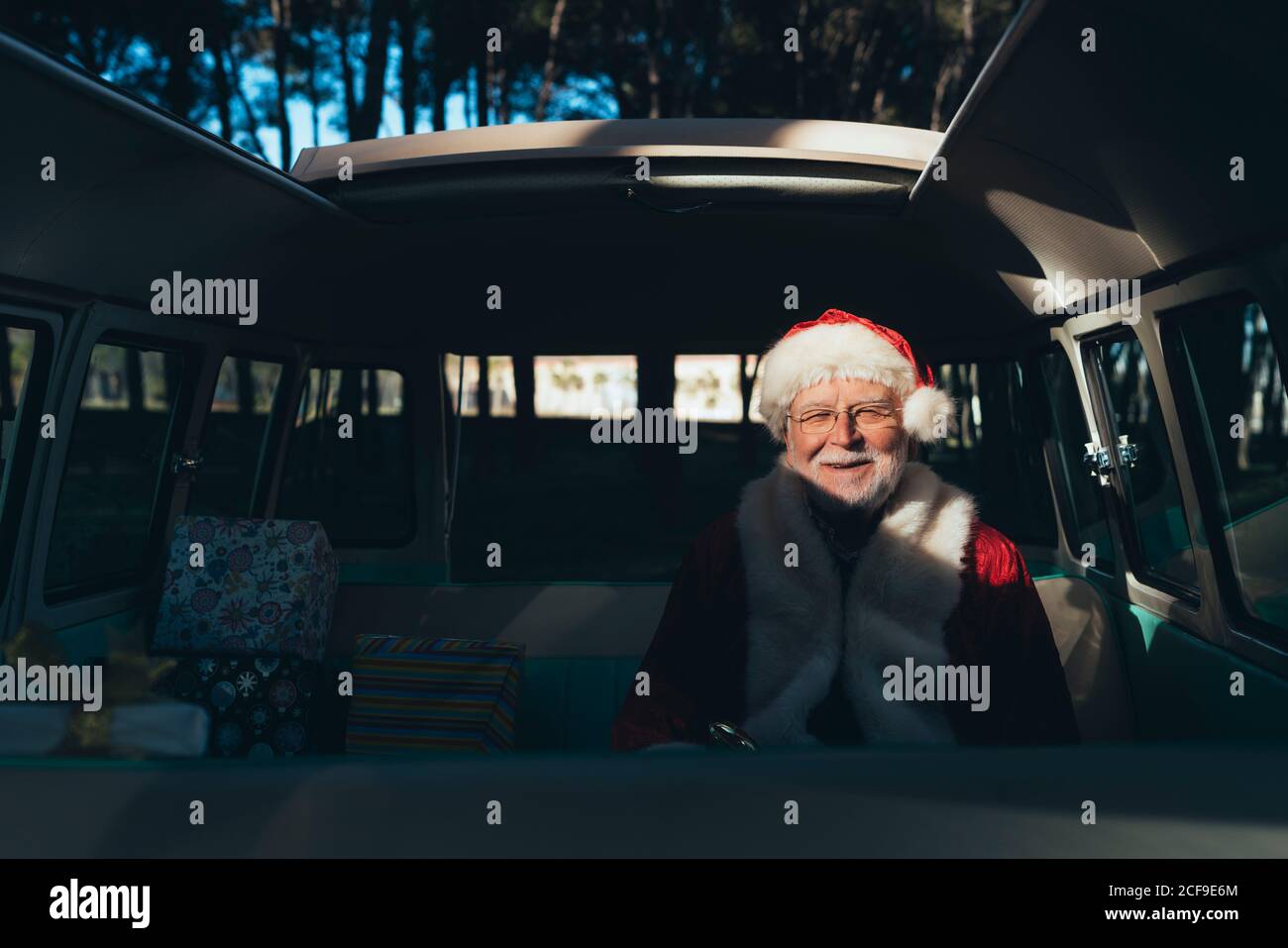 Smiling senior man in costume of Santa Claus sitting in a old van near ...