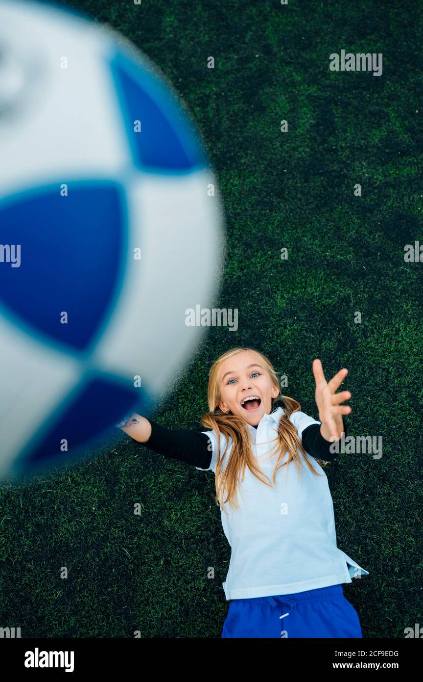 From above joyful preteen girl in white and blue uniform throwing ...