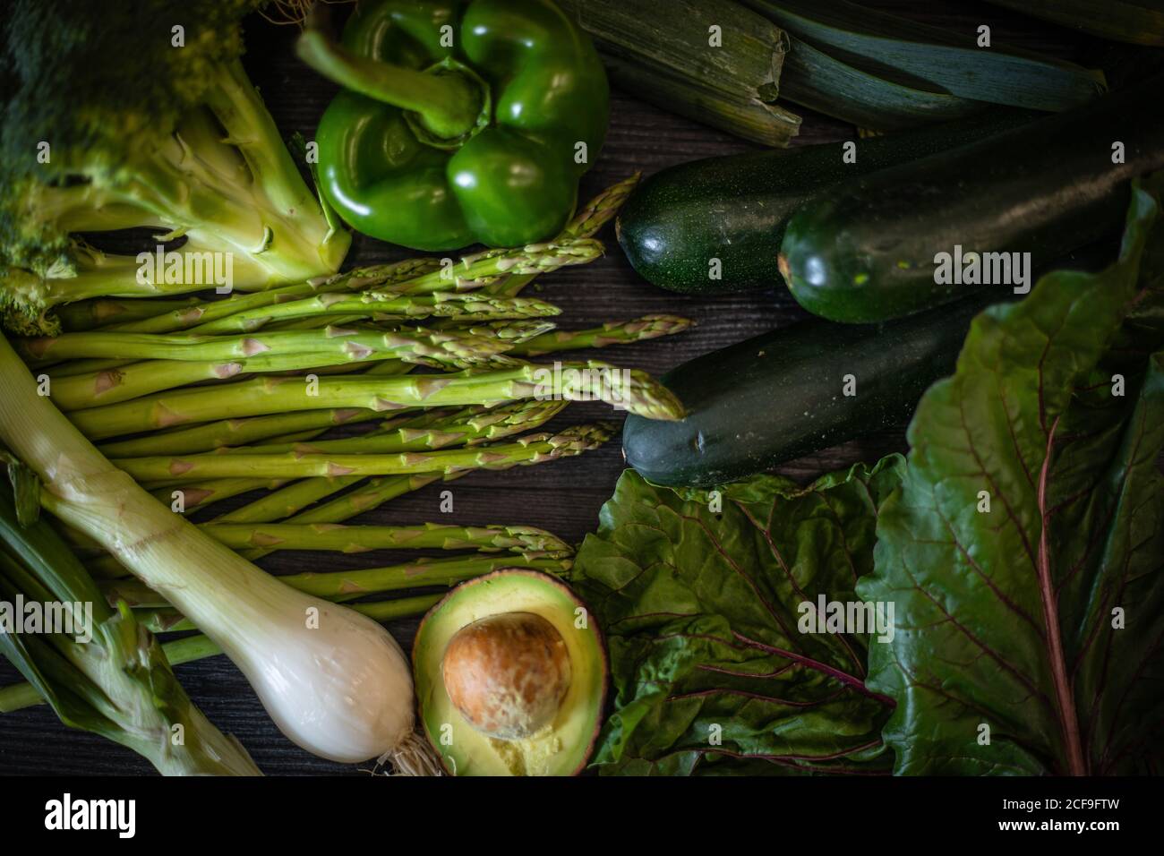 Bunch of various green vegetables placed on dark wooden table on black ...