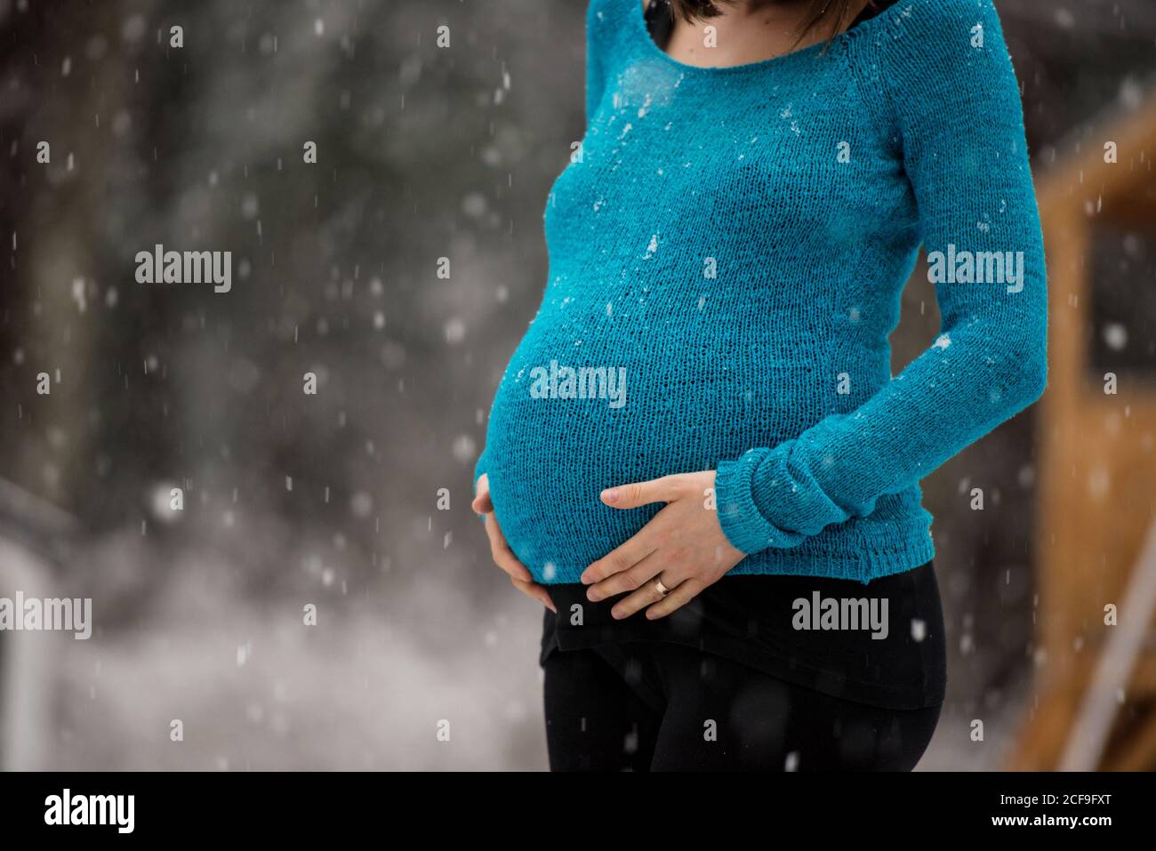 Closeup view of a pregnant woman in blue sweater standing outside on a ...