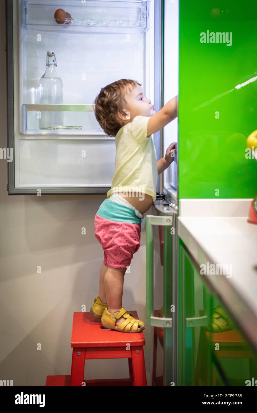 Side view of cute little child standing on stool and taking food from ...