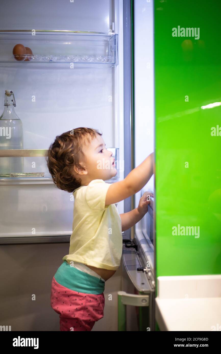 Side view of cute little child standing on stool and taking food from ...