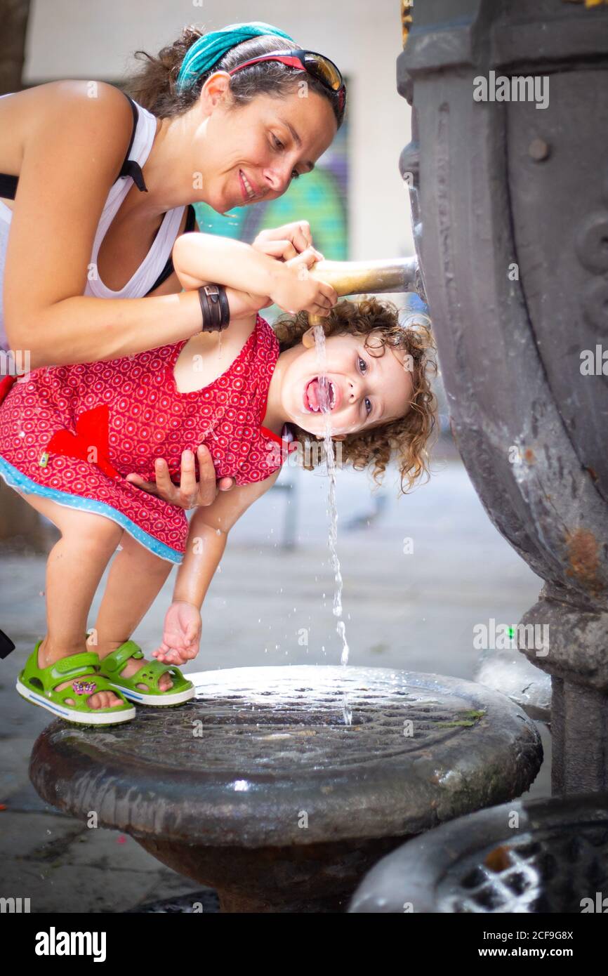 Happy mother pouring water from drinking fountain for funny girl with ...