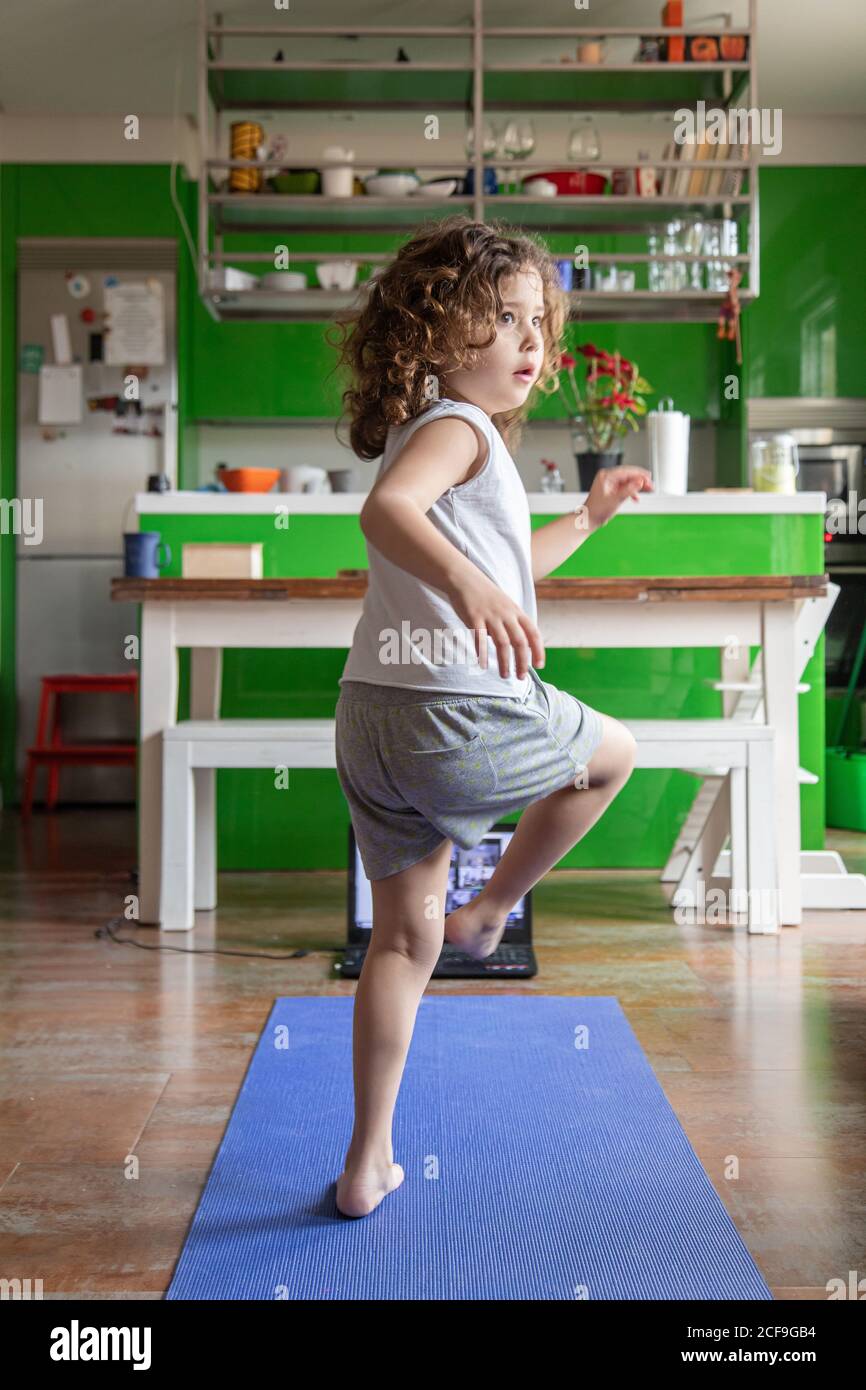 Back view of little girl in activewear learning balance yoga asana ...