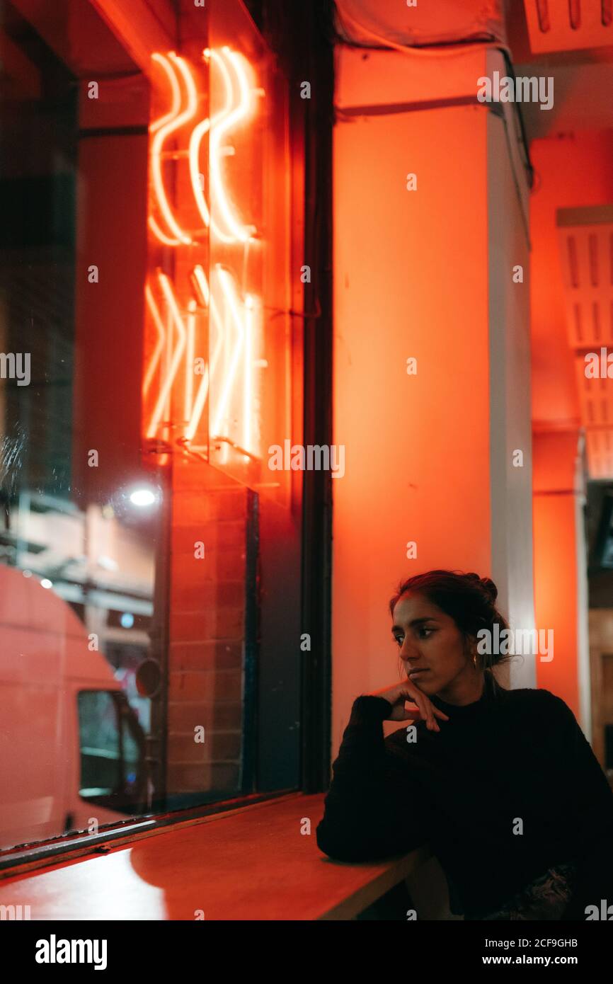 Gorgeous young ethnic Woman looking out window with red lightening on ...