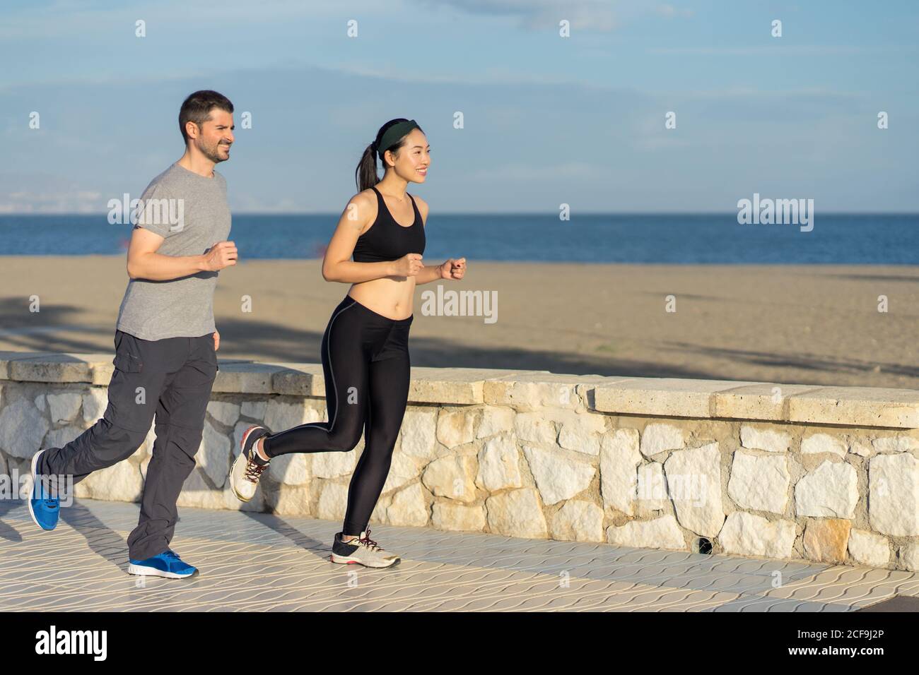 Healthy content couple in sports clothing smiling while jogging by the ...