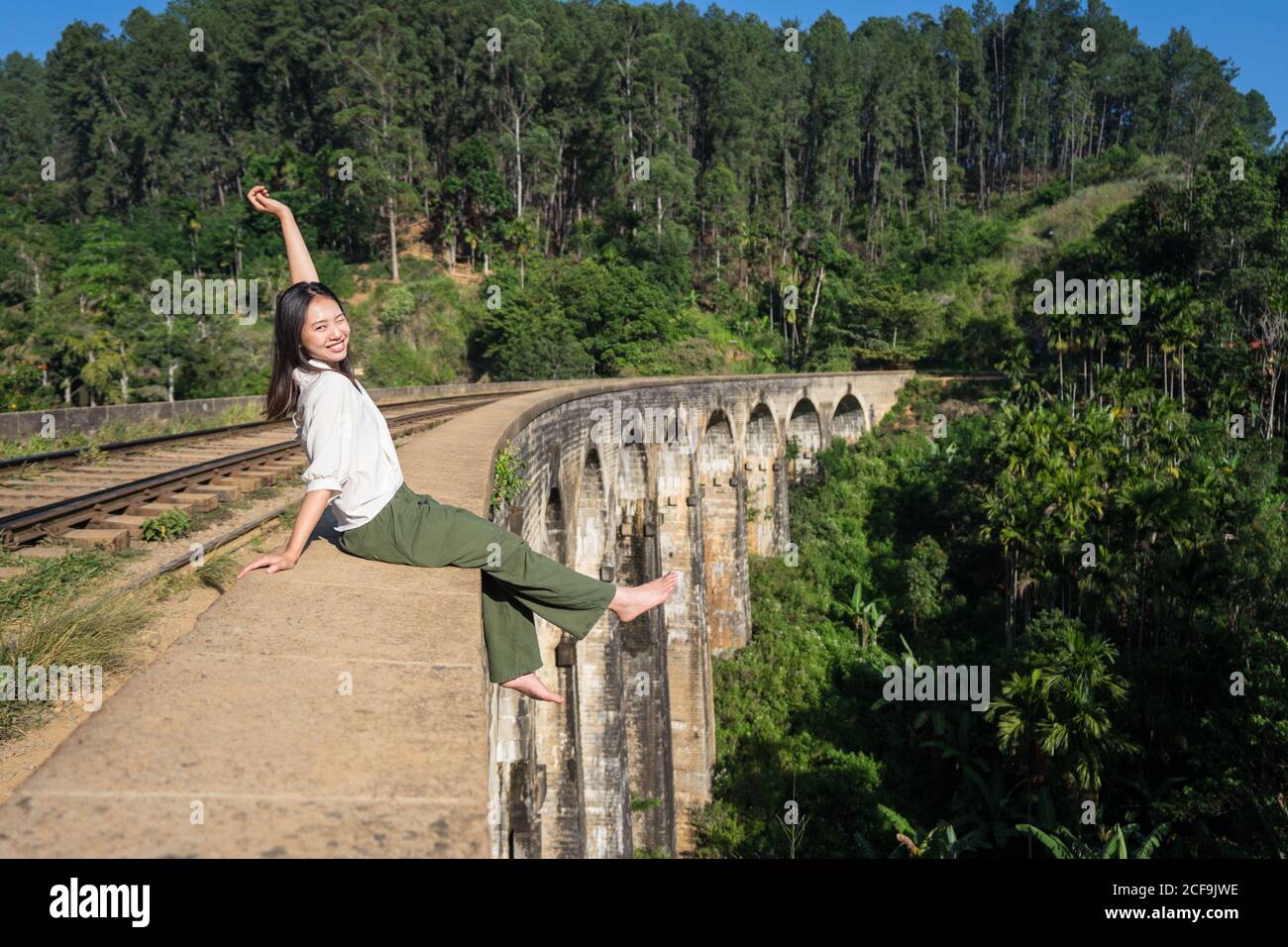Relaxed Asian Woman sitting on bridge dangling legs and waving hand ...