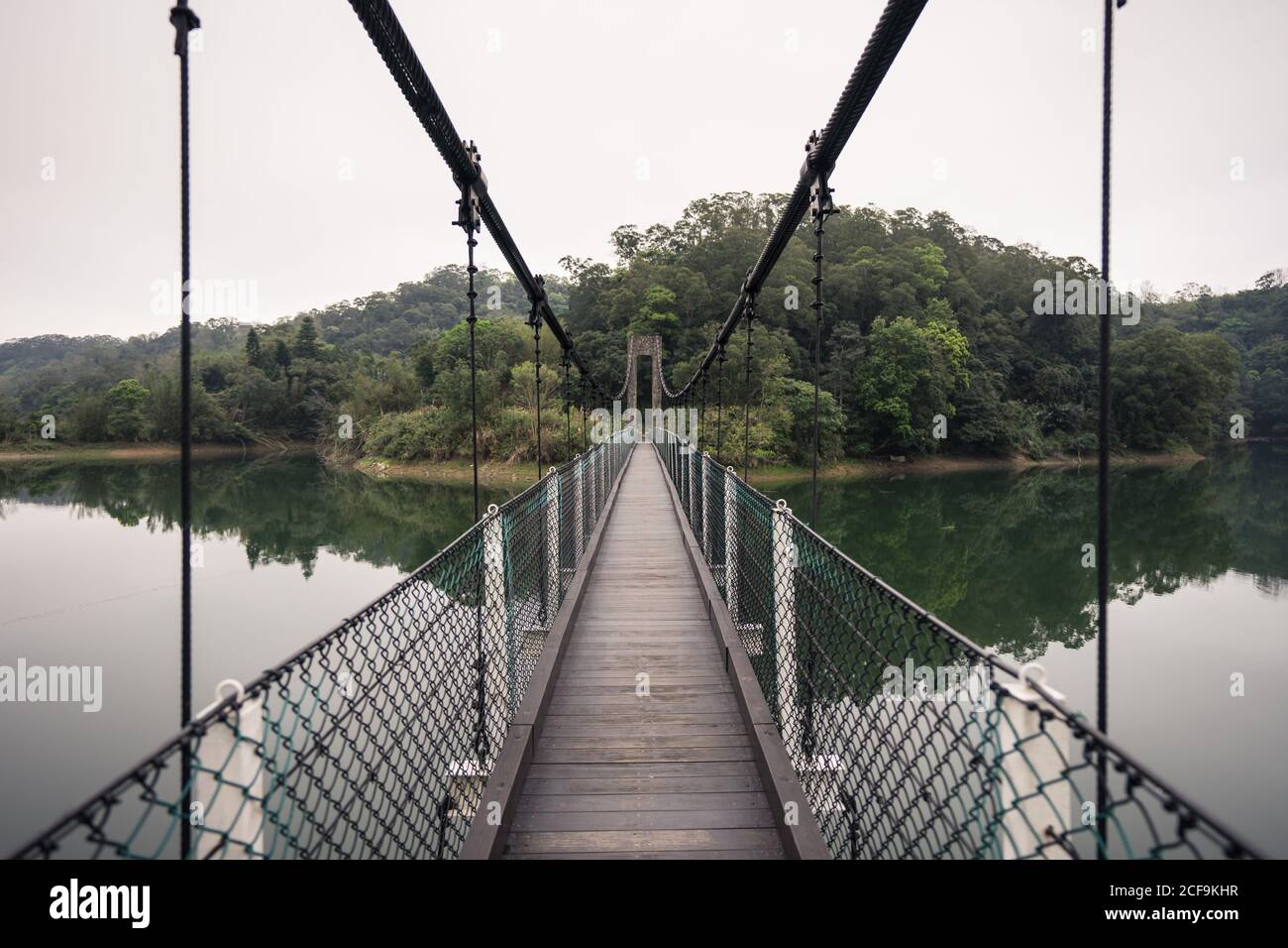 Suspension bridge with wooden floor and metallic grid over large lake ...