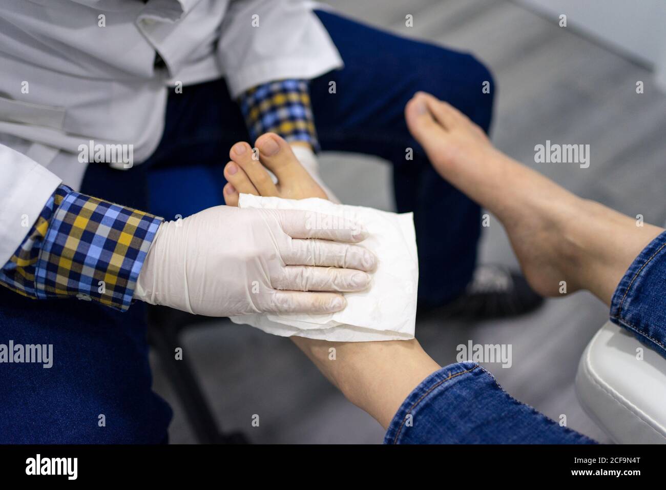 Crop male podiatry doctor in protective gloves cleaning foot of female ...