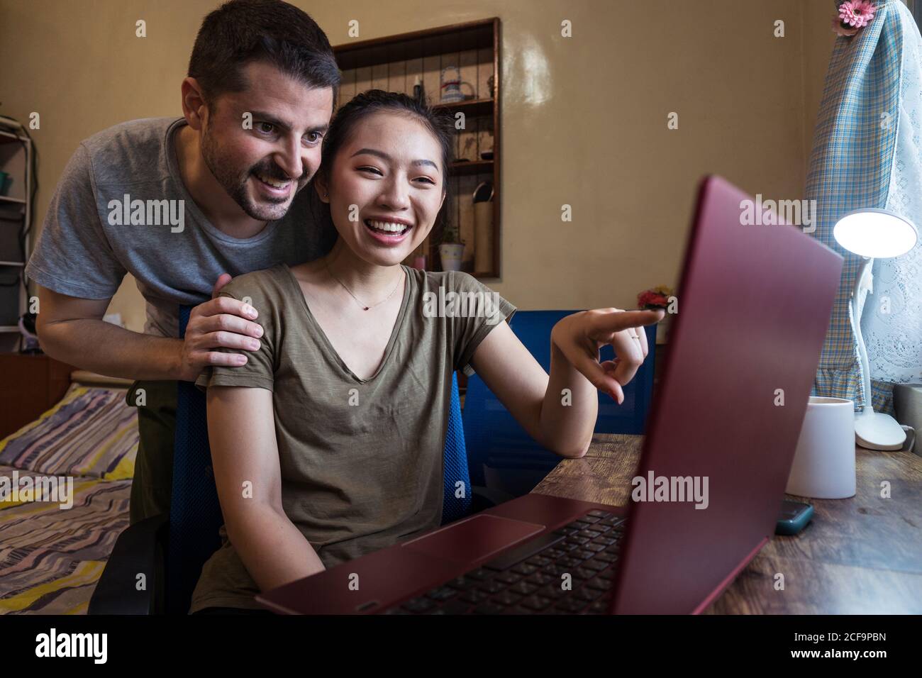 Low angle of happy boyfriend helping asian girlfriend working on the ...