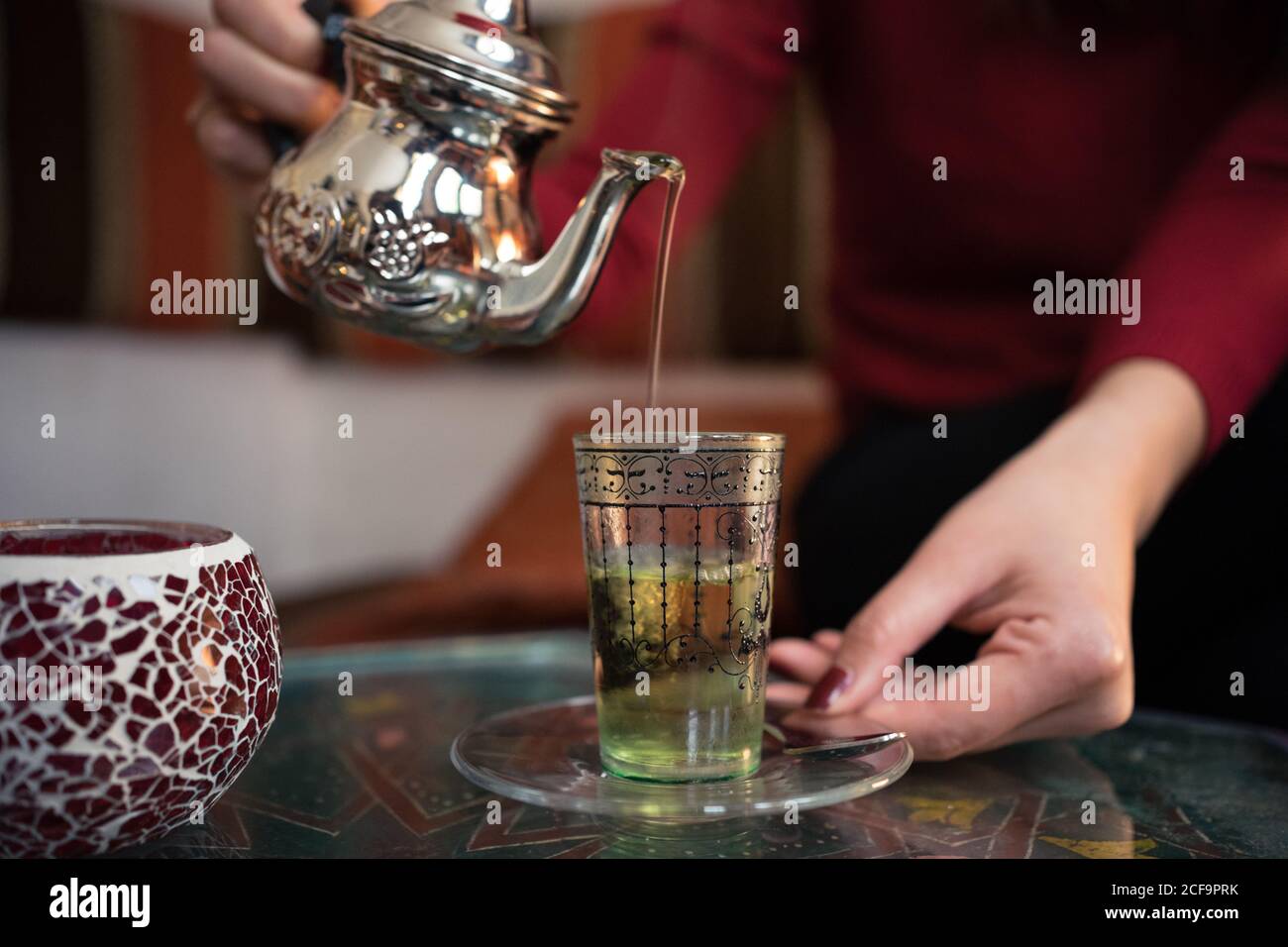 Happy ethnic female pouring fresh Arabic tea in cup while sitting on ...
