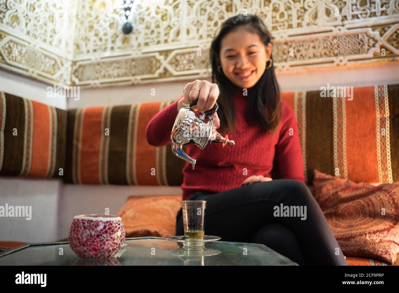 Happy ethnic female pouring fresh Arabic tea in cup while sitting on ...