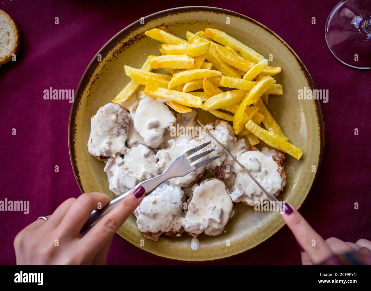Top view of crop lady with fork and knife eating fries with meat in ...
