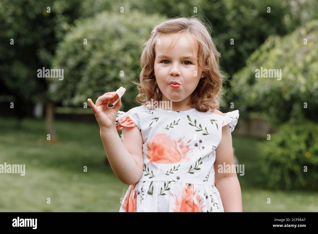 Funny kid girl eating sandwich outdoors. Having fun. Looking at camera ...