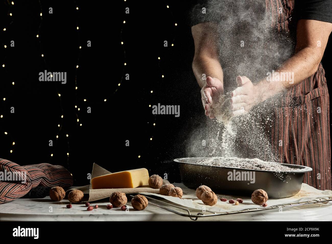 Crop anonymous male baker in apron spilling flour over baking pan with ...