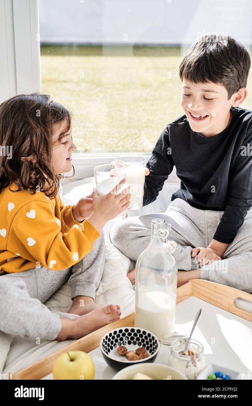 Cheerful kids in pajamas sitting with crossed legs near tray with ...