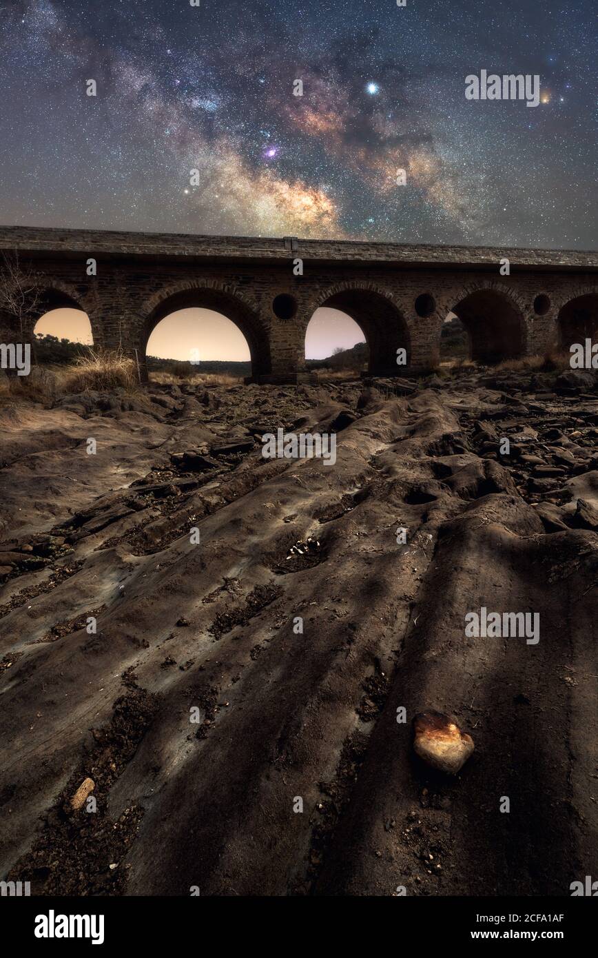 Rocky ground and old stone bridge with colorful night sky with milky ...