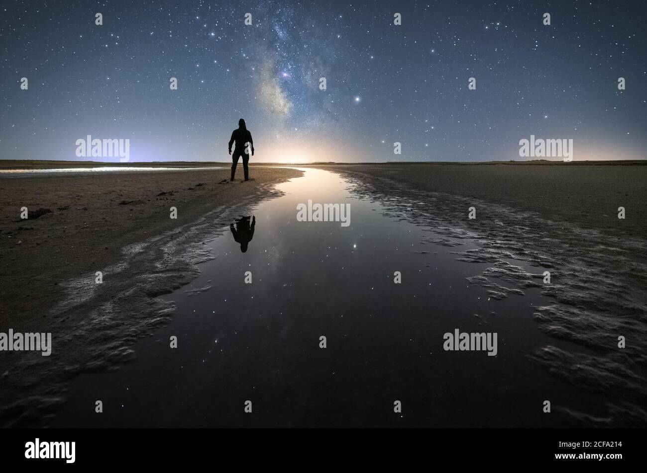 Back view of anonymous man standing on empty road among calm water and ...