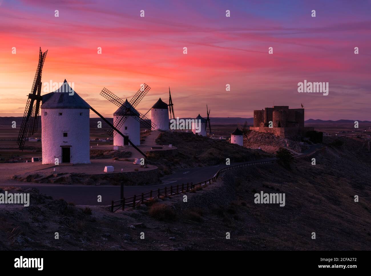 Ancient windmills and aged castle against bright sunset sky in evening ...
