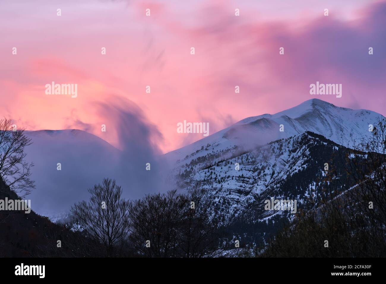 Sharp mountain peaks covered partially with snow and surrounded by fog ...