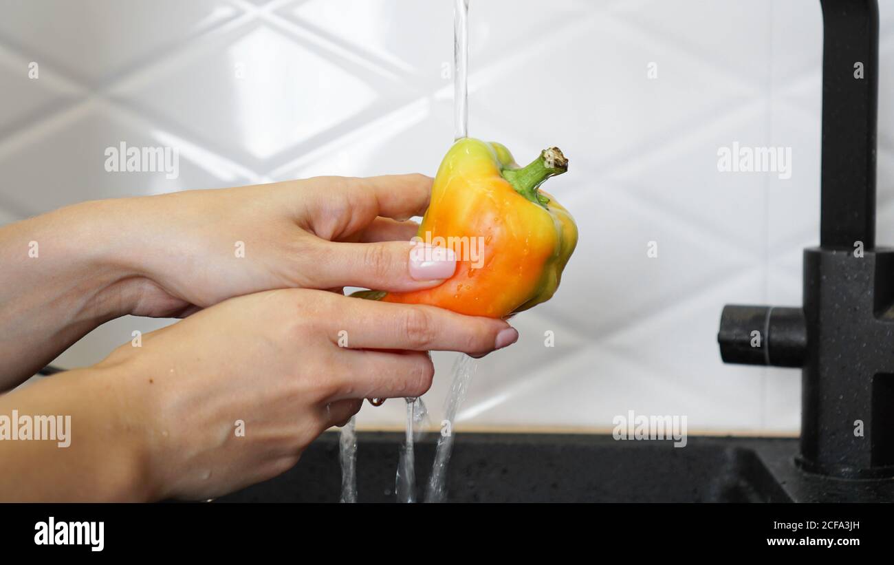 Female hands washing yellow and red color pepper. White kitchen ...