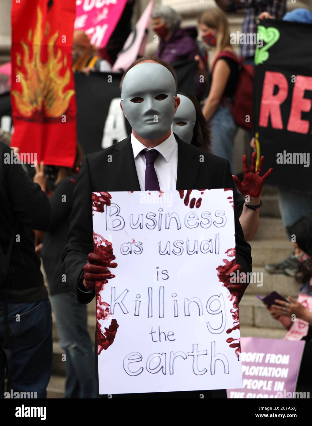 A masked protester, hands covered with fake blood, holds a placard ...