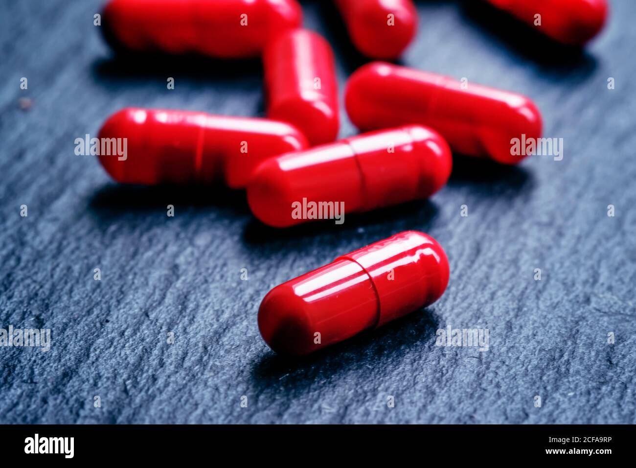 Red pills in capsules of anemia on a black table, selective focus ...