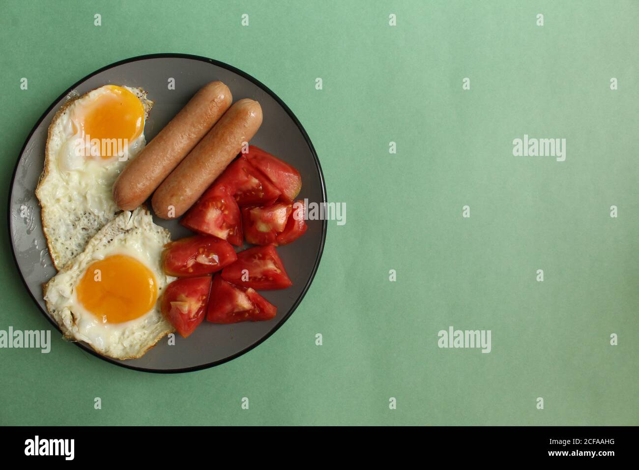 Breakfast food on a gray plate on a green background sausages tomatoes ...