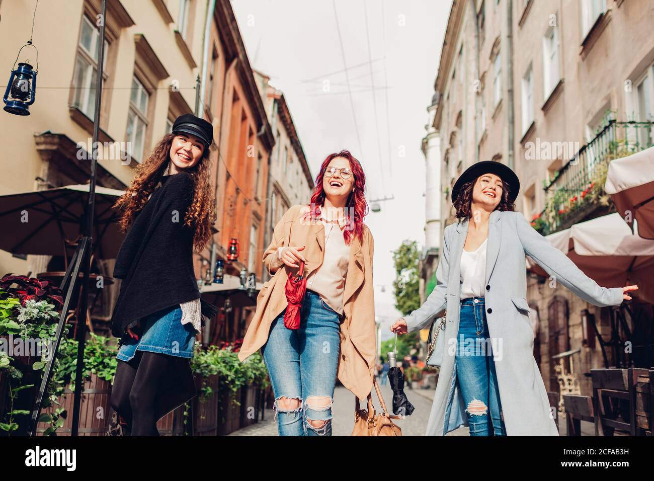 Three young women walking on city street laughing. Girls friends ...