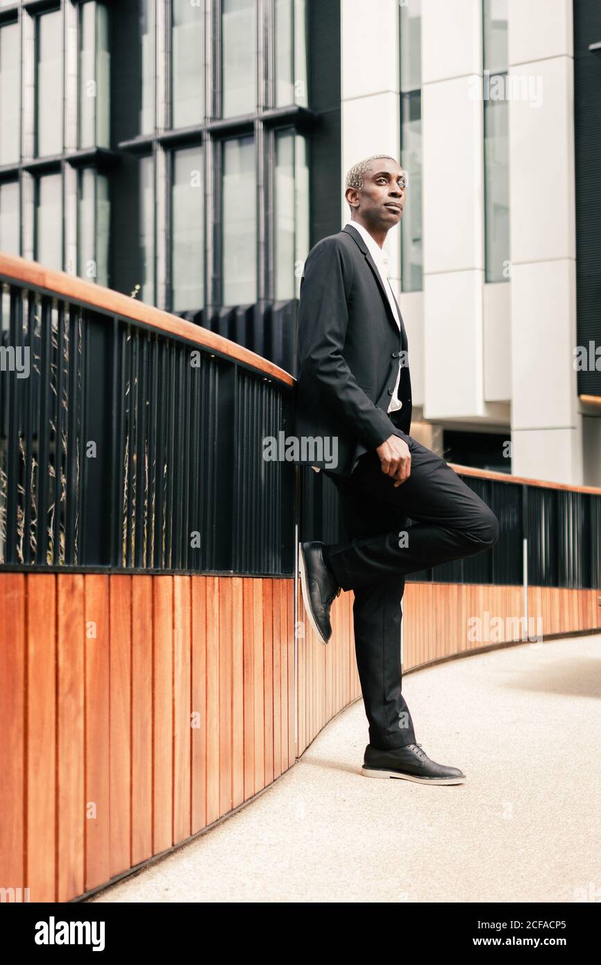 Confident black businessman leaning on railing Stock Photo - Alamy