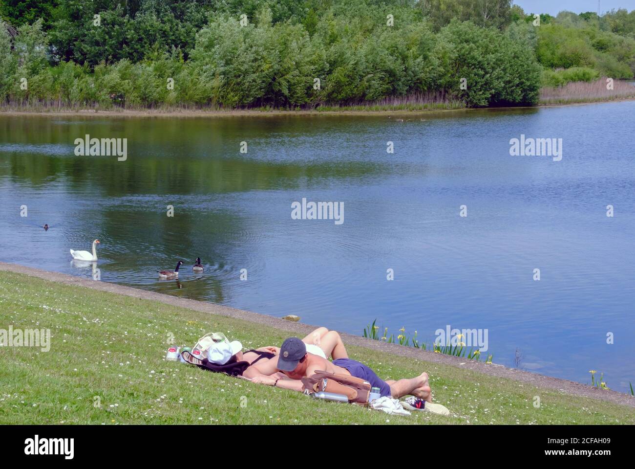 Young couple lie on the grass next to the water at Ruislip Lido ...
