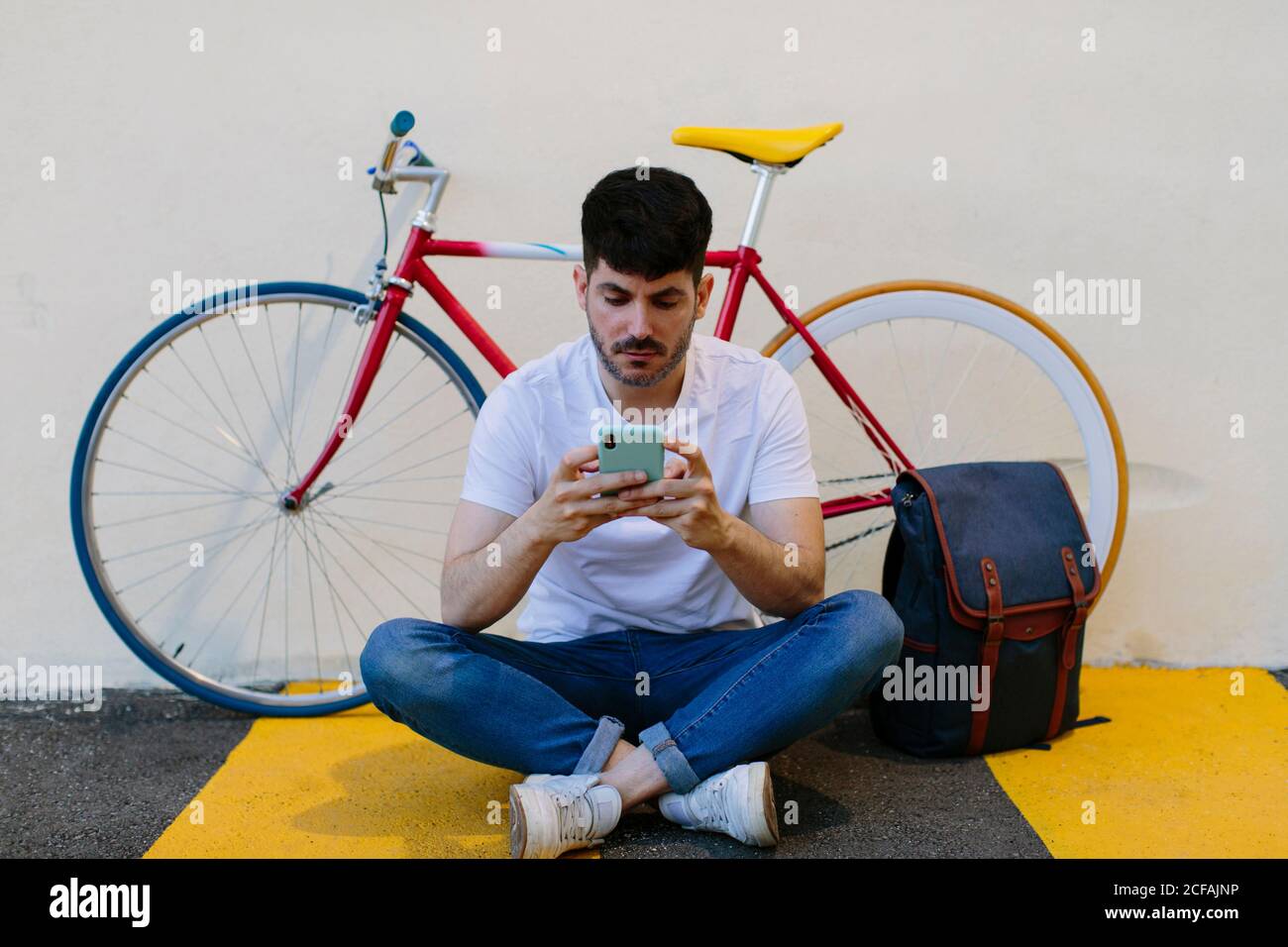 man checking his smartphone. He is sitting on the floor with a bike and ...