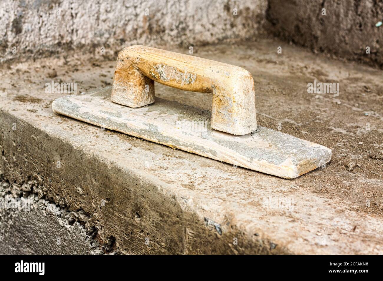 Wooden trowel used for masonry on a rough unfinished concrete surface ...