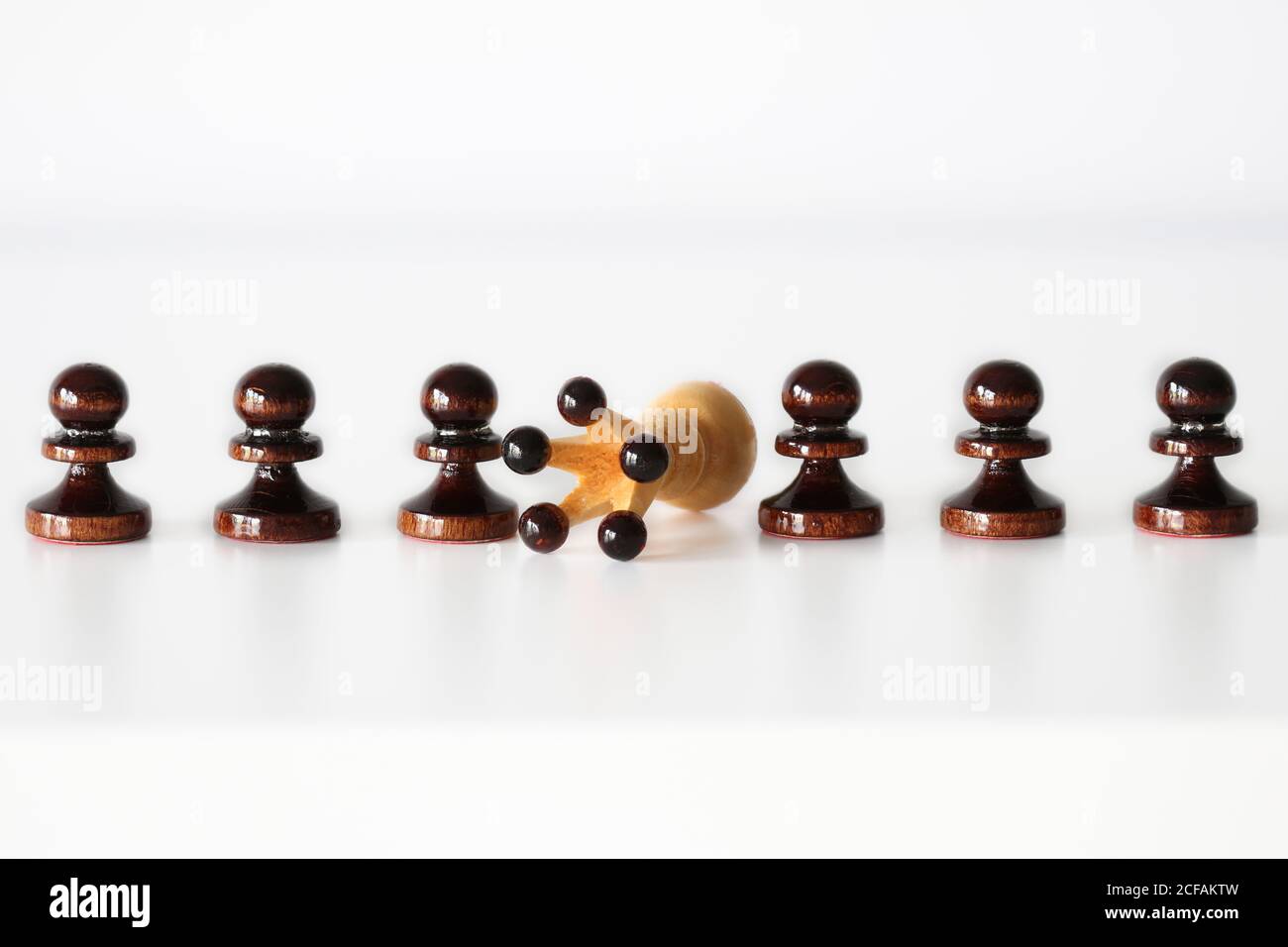 Row of black pawn chess pieces with knocked down white queen in the ...