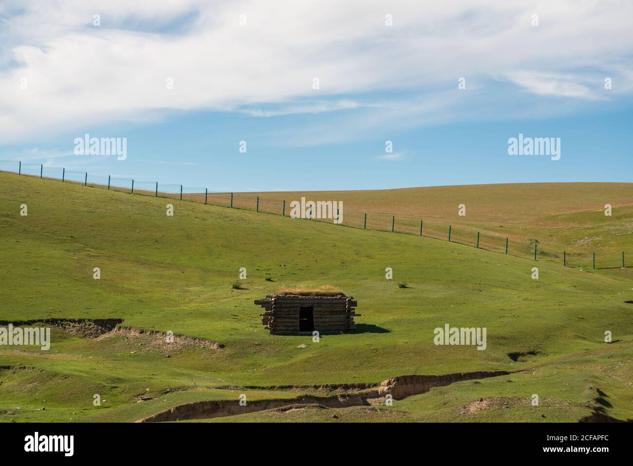 Small cabin located on grassy slope and surrounded by fence on sunny ...