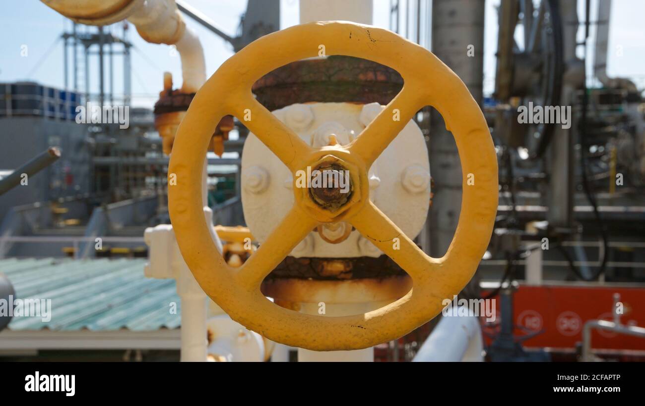 Large yellow rusty painted metal round valve wheel connecting white LNG ...