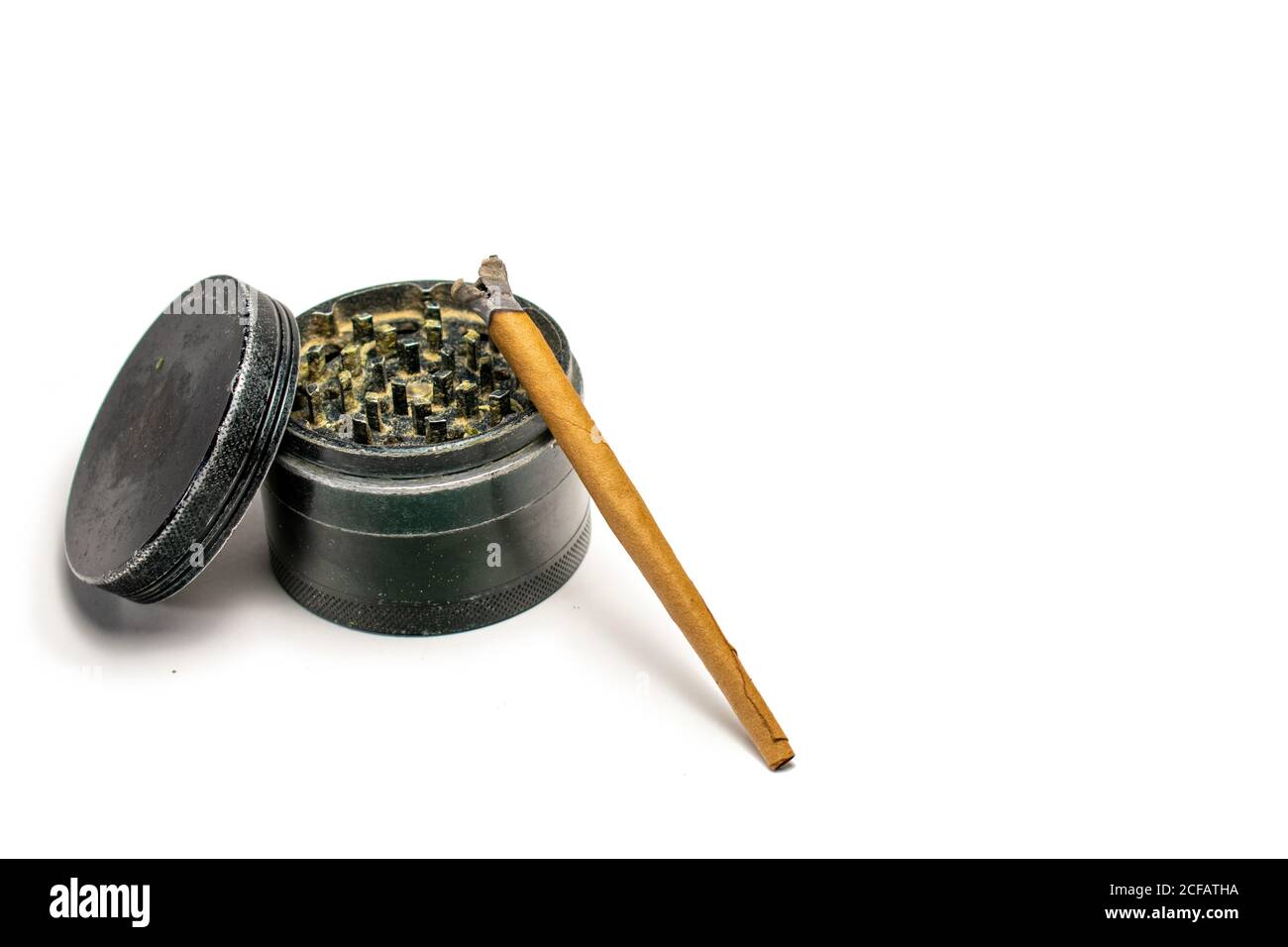A Lit Cannabis Cigar Leaning on a Black Grinder With the Lid Leaning on ...
