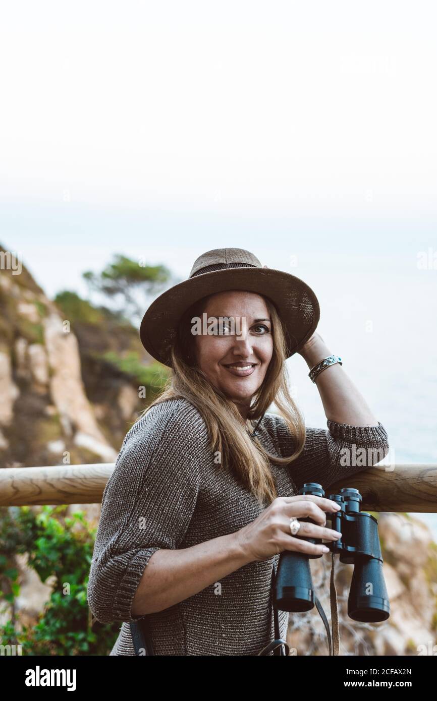 Adult Woman observing view with binocular while standing at fence on ...