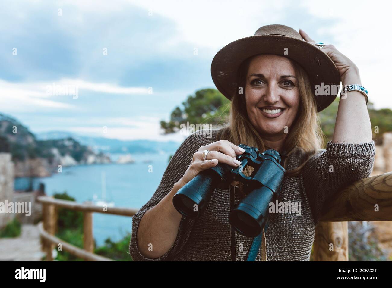 Adult Woman observing view with binocular while standing at fence on ...