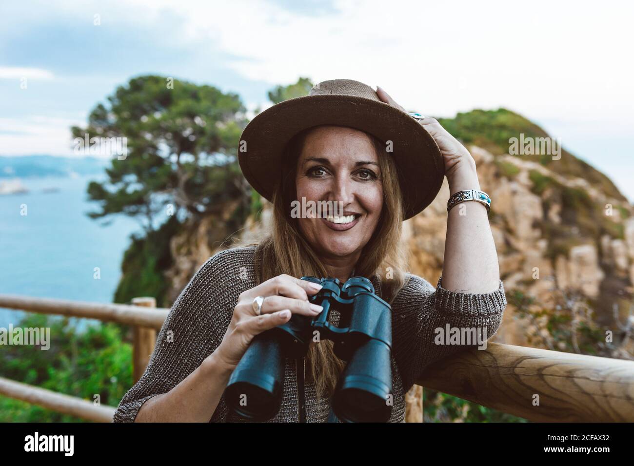 Adult Woman observing view with binocular while standing at fence on ...