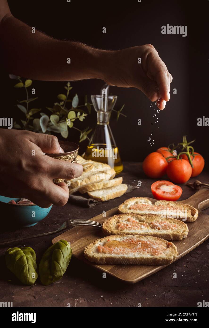 unrecognizable person spilling salt of pieces of fresh bread with sauce ...