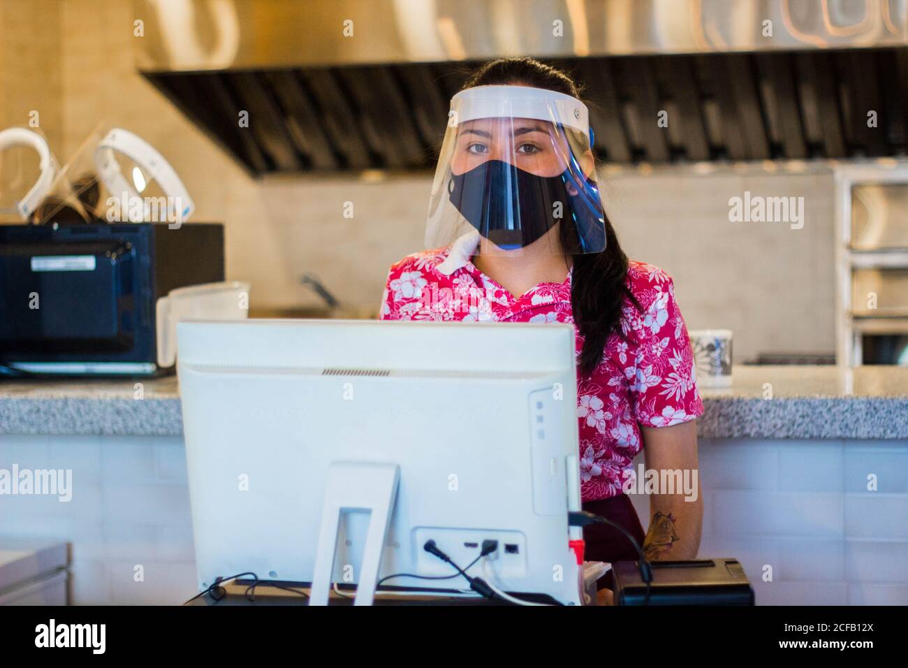 Shallow focus of a female cashier wearing a facemask and a face shield ...