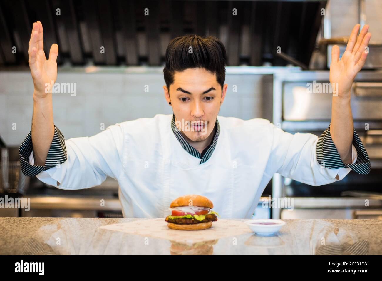 Male cook looking at a burger shocked with hands up Stock Photo - Alamy