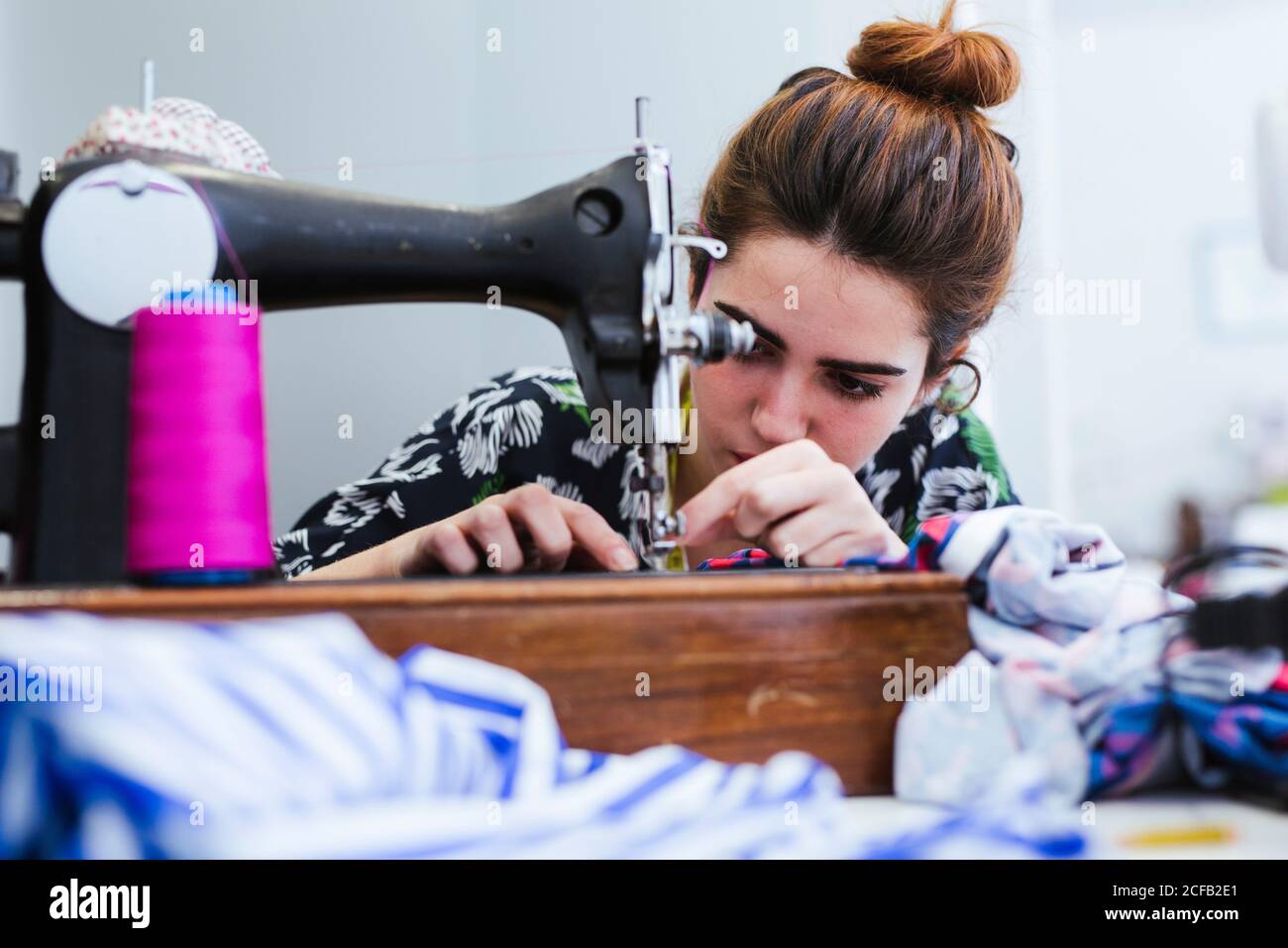Teenage girl student practicing sewing on modern machine in cozy ...