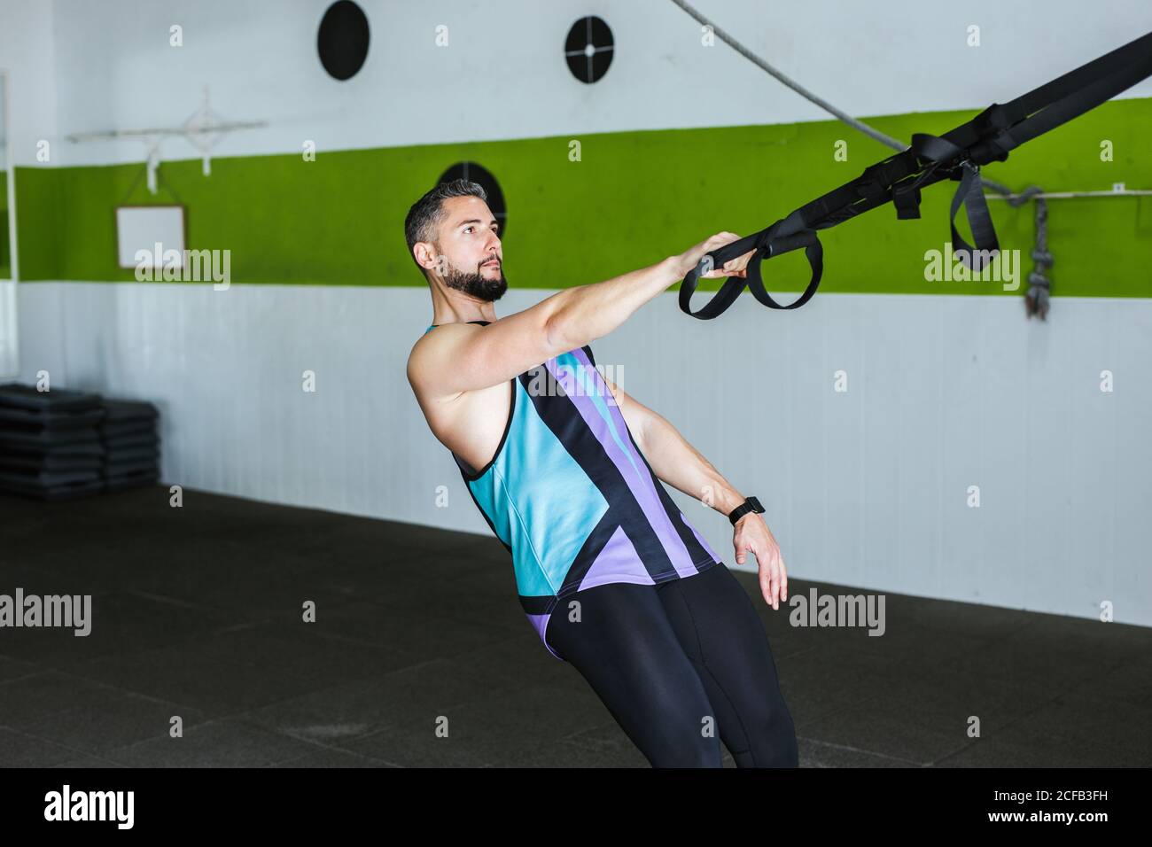 Side view of young muscular man in sportswear training with elastic ...