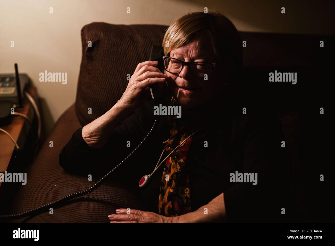 Glad elderly lady smiling and answering phone call while sitting in ...